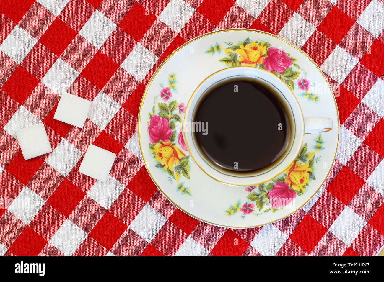 Black tea in vintage porcelain cup, sugar cubes on red and white ...