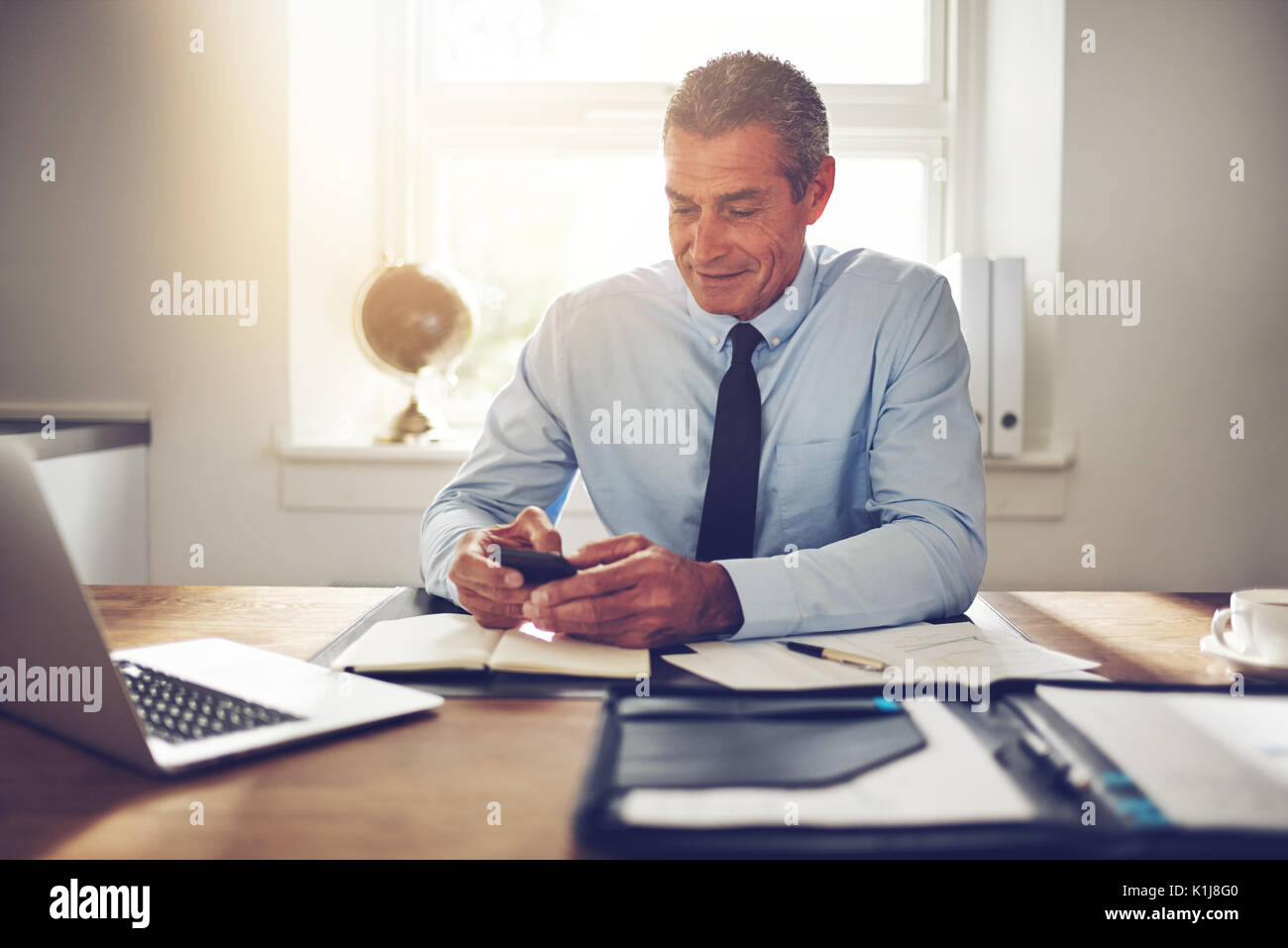 Smiling mature businessman reading text messages on his cellphone while ...