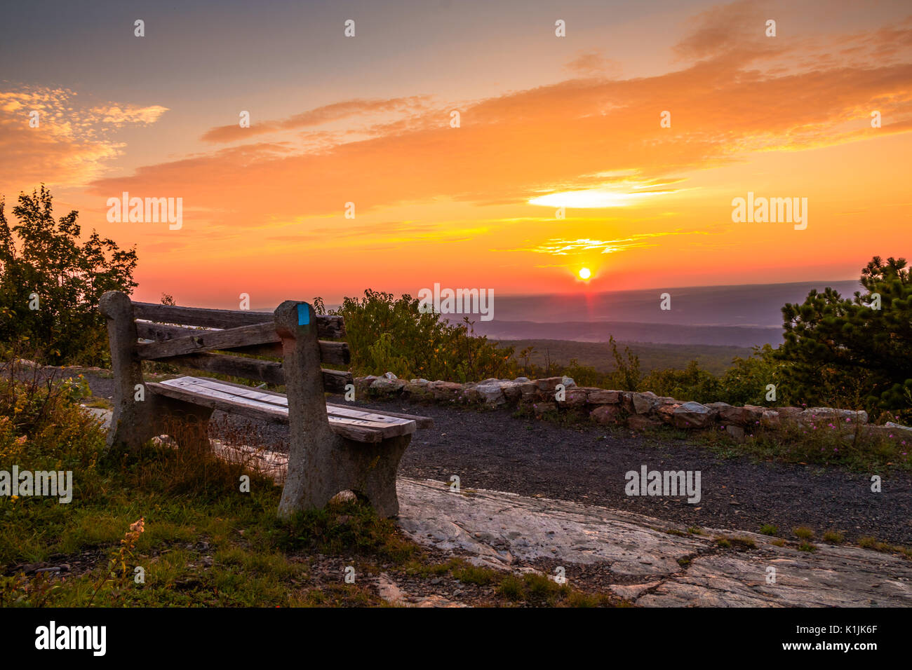 Lone bench faces majestic sunset in early fall as the sun sets at the ...