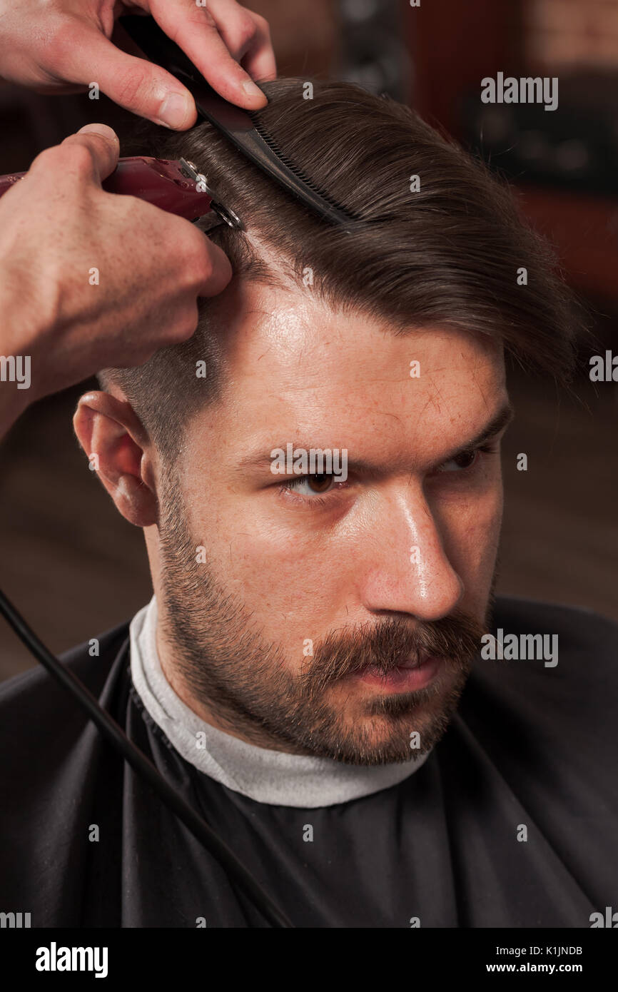 The hands of barber making haircut to young man in barbershop Stock ...