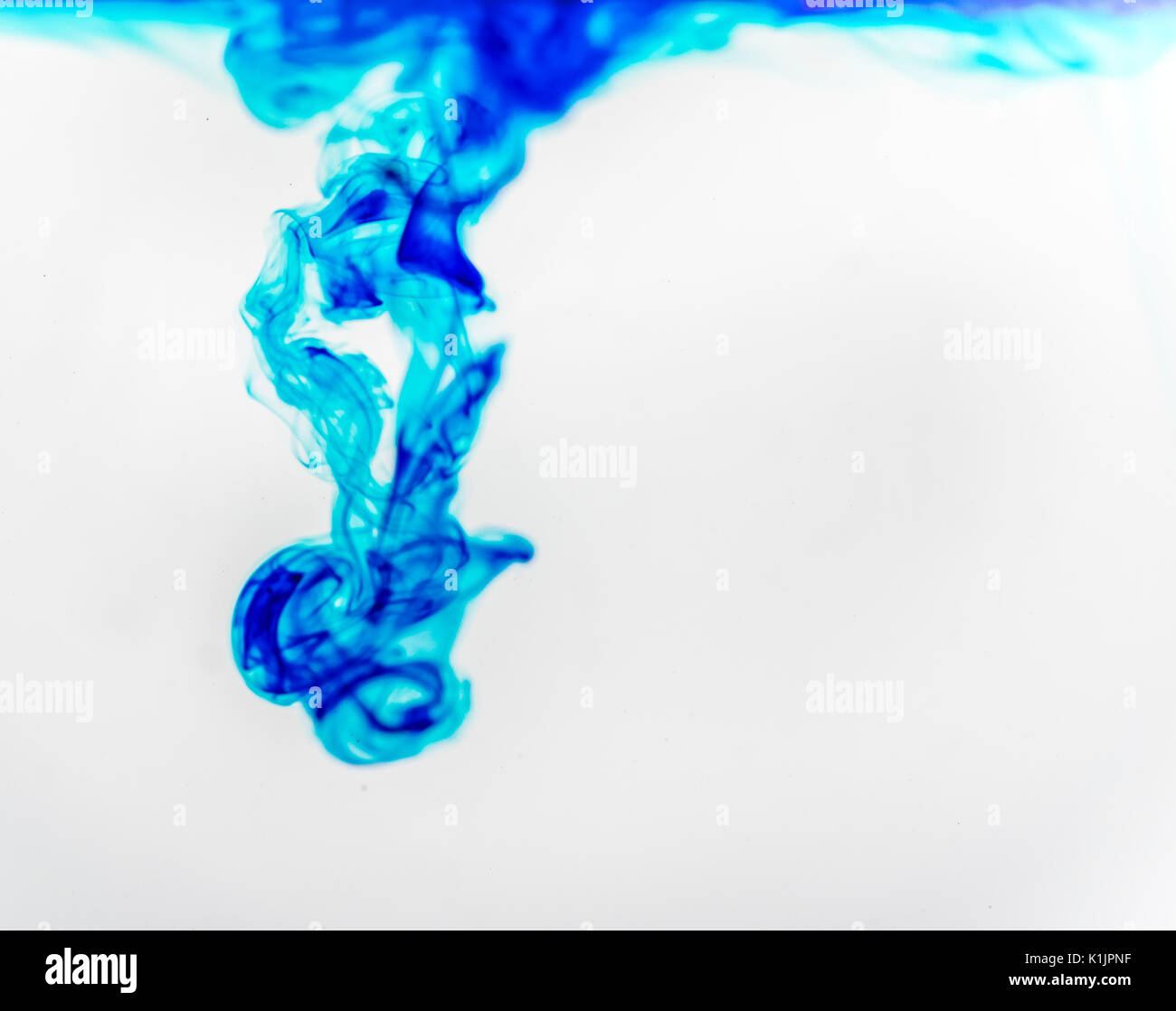 Abstract Blue liquid ink dye, mixing on water, over a white backlit ...