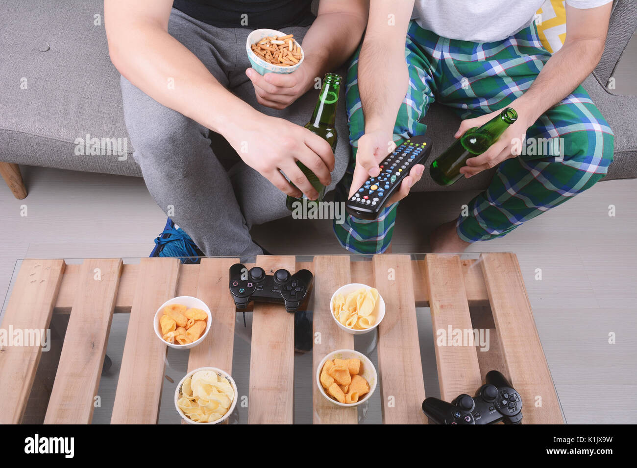 Portrait of two friends playing videogames, eating snacks and drinkng ...
