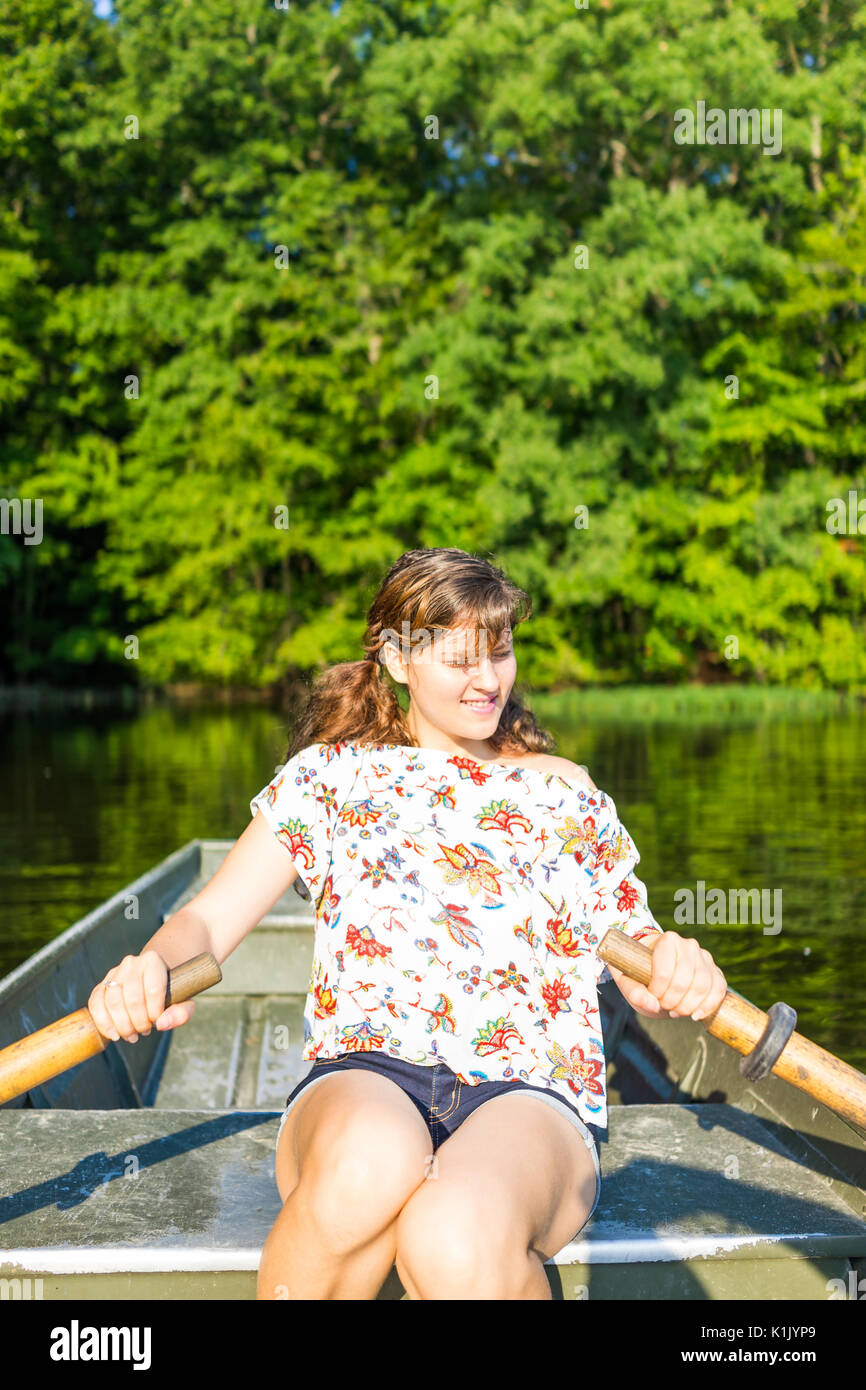 Happy smiling young woman rowing boat on lake in Virginia during summer ...