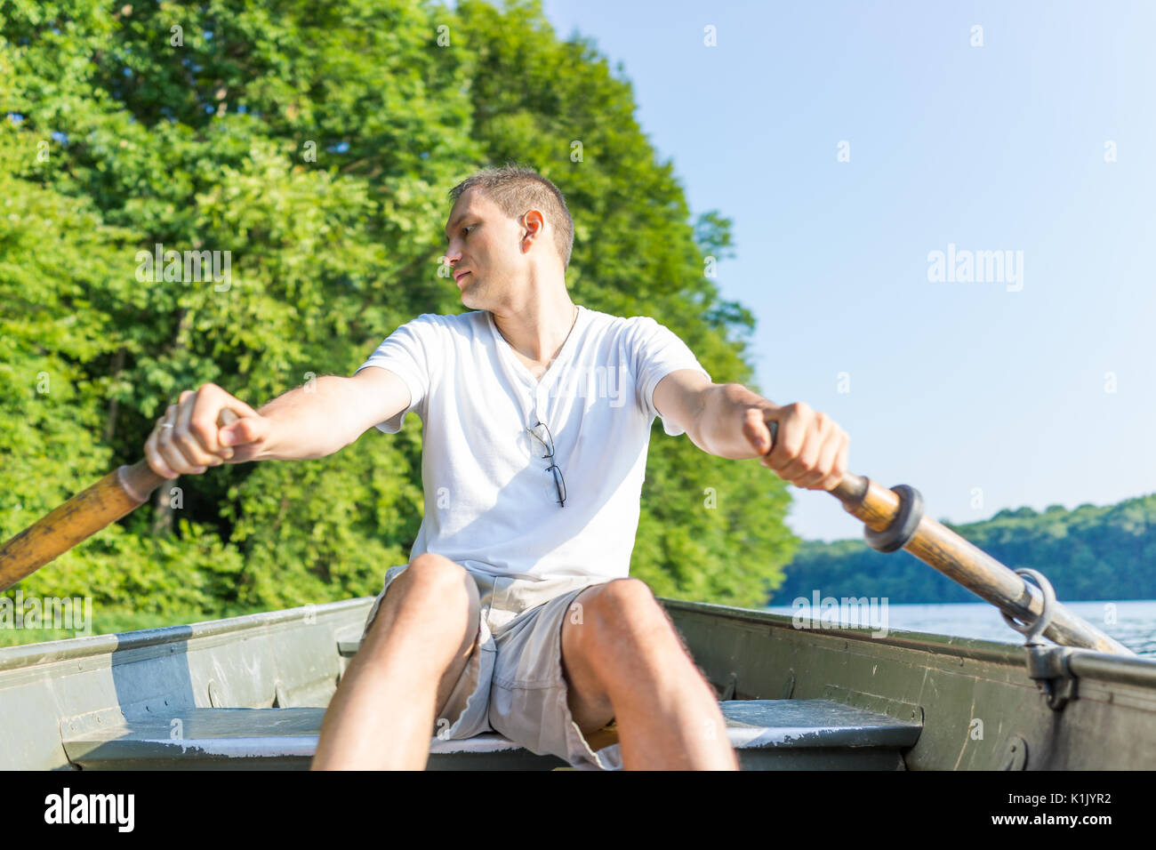 Young man rowing boat on lake in Virginia during summer in white shirt ...