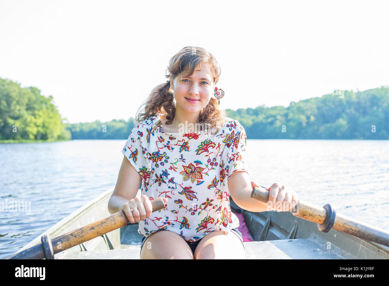 Happy smiling young woman rowing boat on lake in Virginia during summer ...