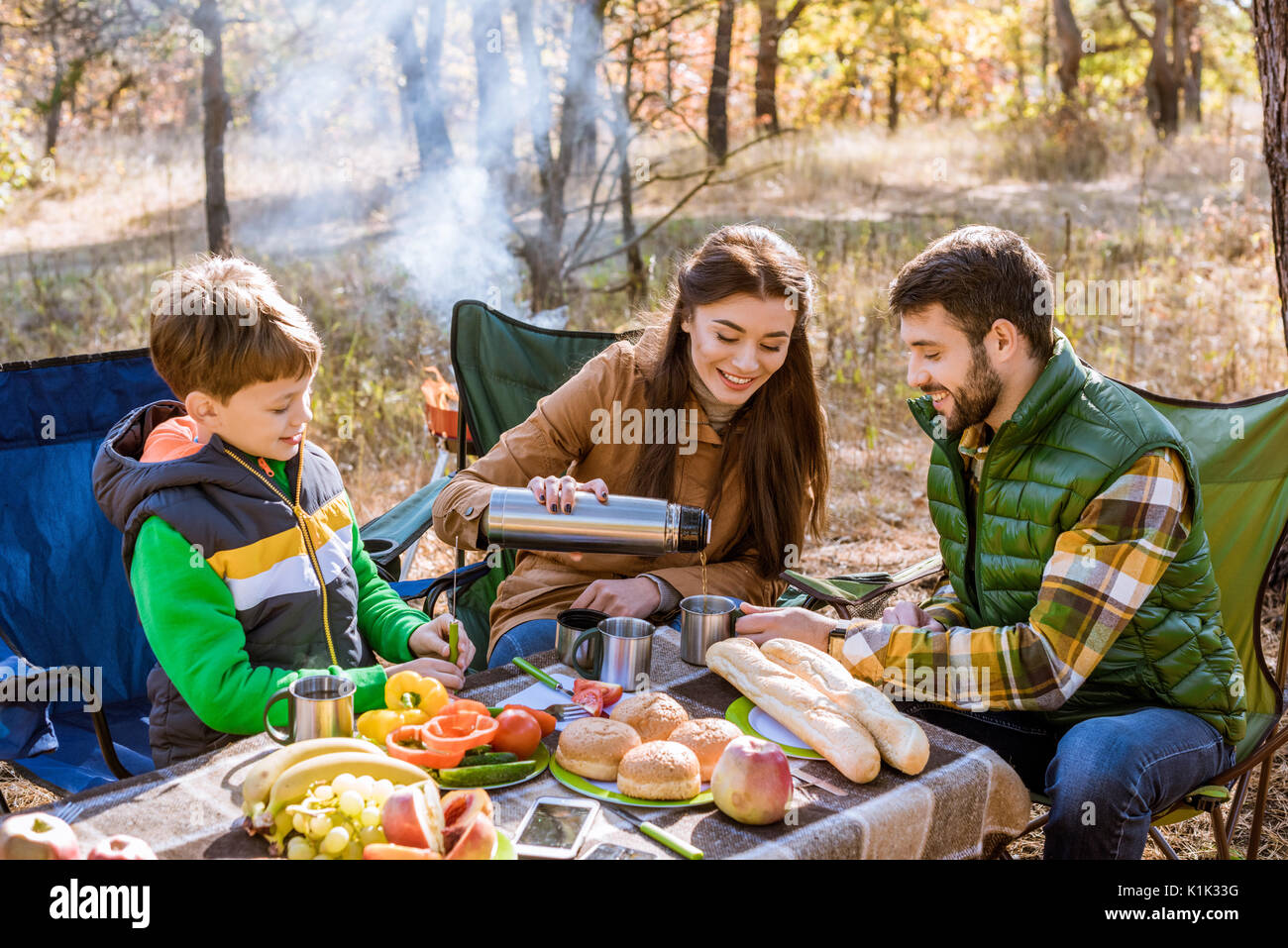 Happy smiling family drinking tea while sitting at table on picnic in ...