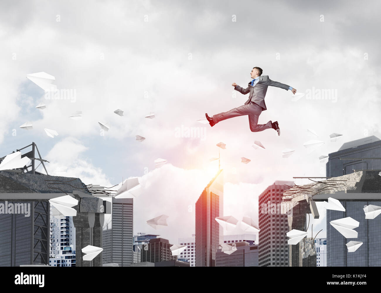 Businessman jumping over gap with flying paper planes in concrete ...