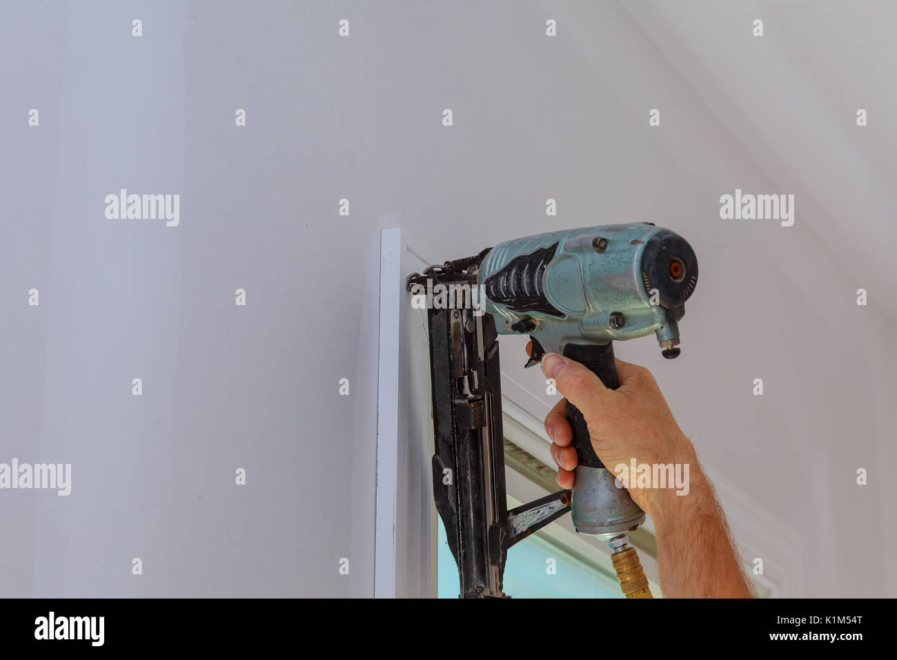 Carpenter using nail gun to moldings on windows, framing trim, with the ...