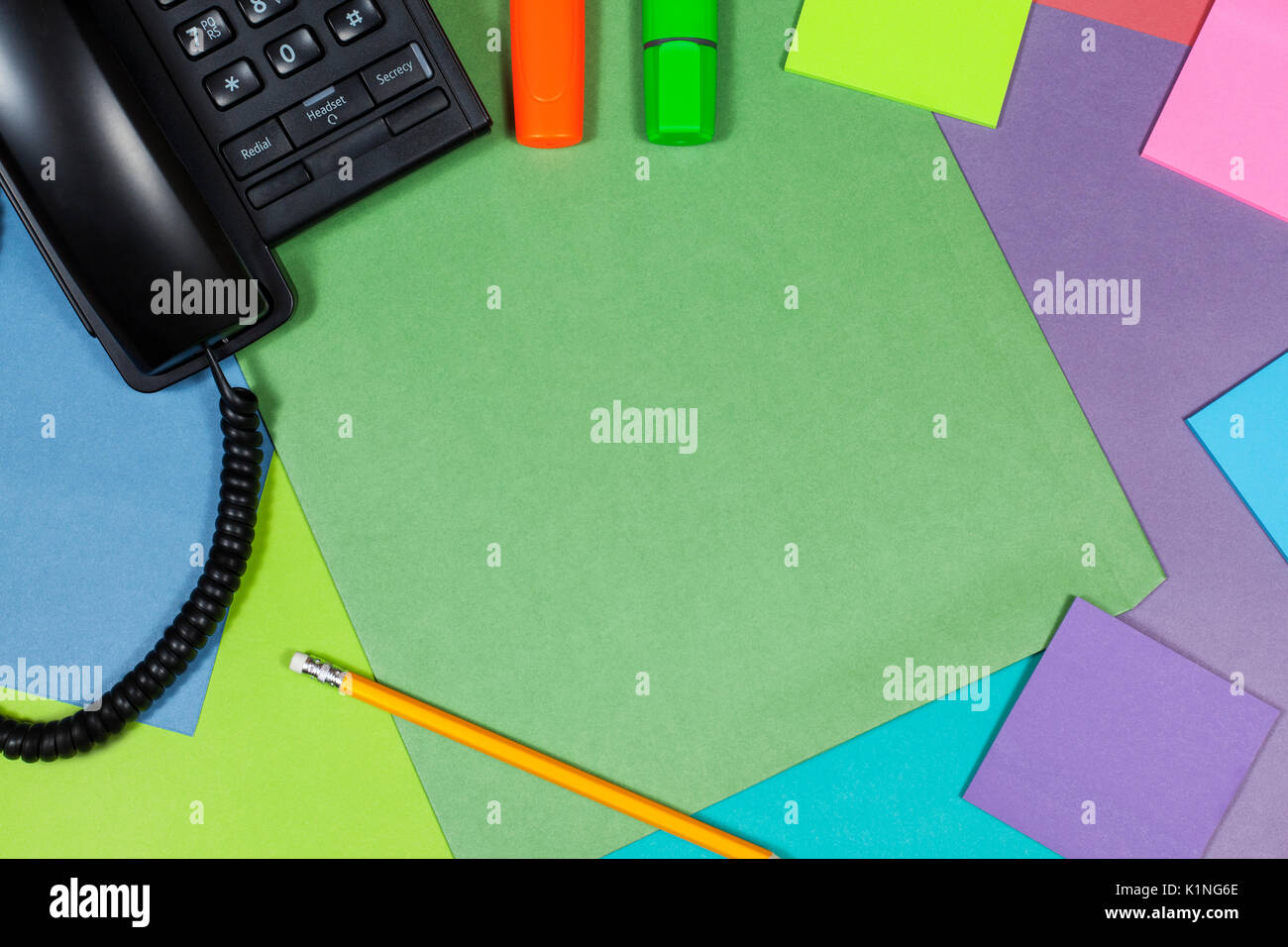 Above view of a colourful desktop with a telephone, highlighter pens ...