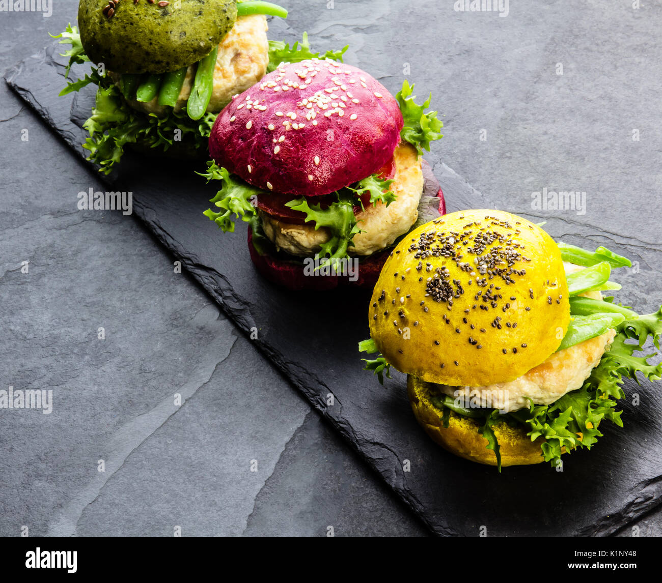 Colored green, yellow and purple burgers on slate board. Top view ...
