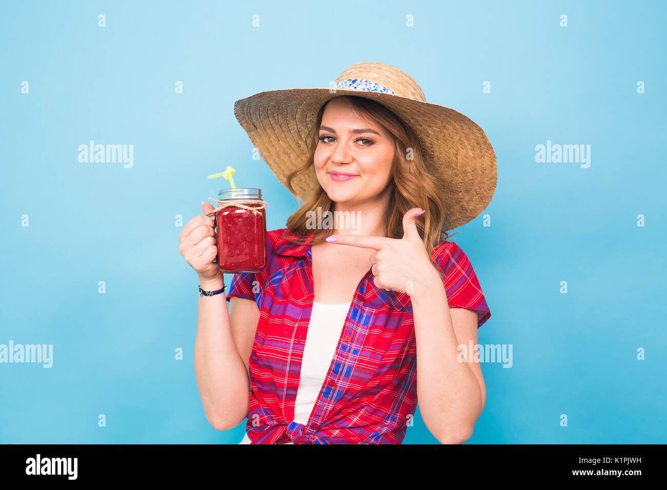 smiling woman drink red juice. studio portrait with blue background and ...