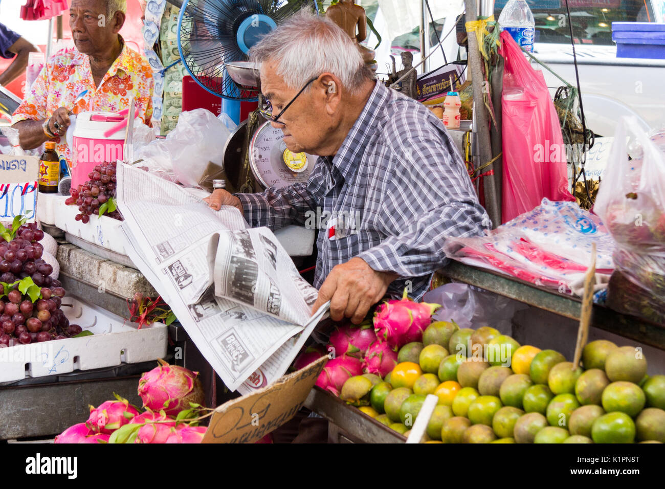 Fruit vendor reading newspaper on market stall, Nonthaburi, Thailand ...