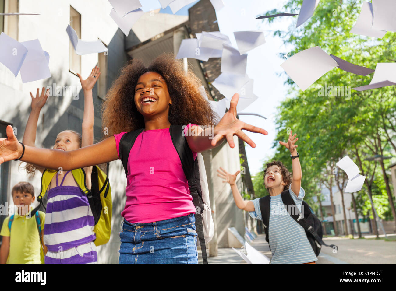 African girl among group of happy kids throwing papers in the air near ...