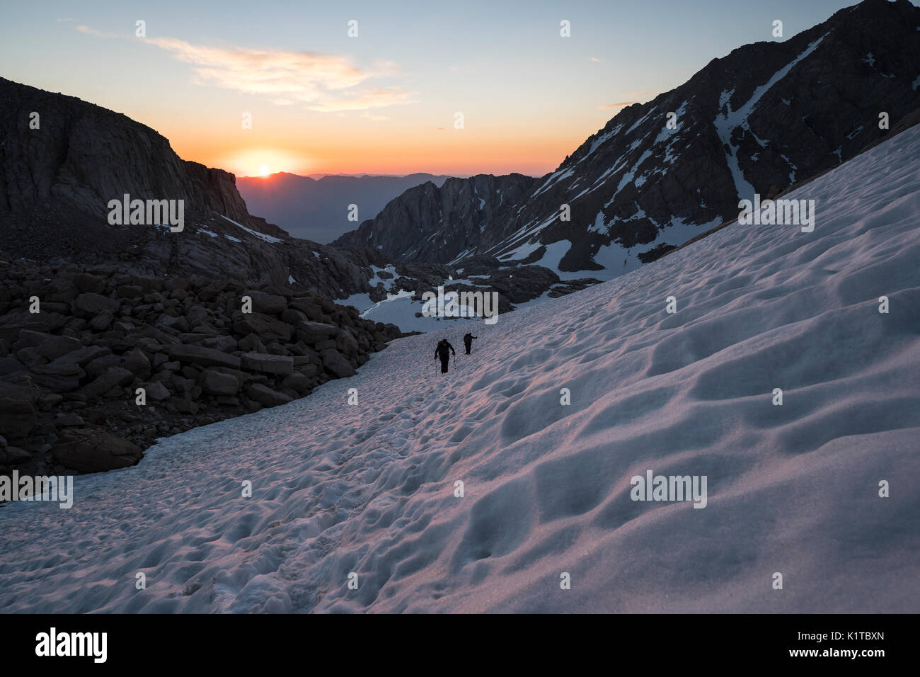 Two hikers cross a snowfield at dawn on the way up towards trail crest ...