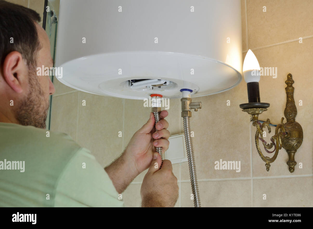Man installing pipes for hot and cold water on a boiler in a bathroom ...