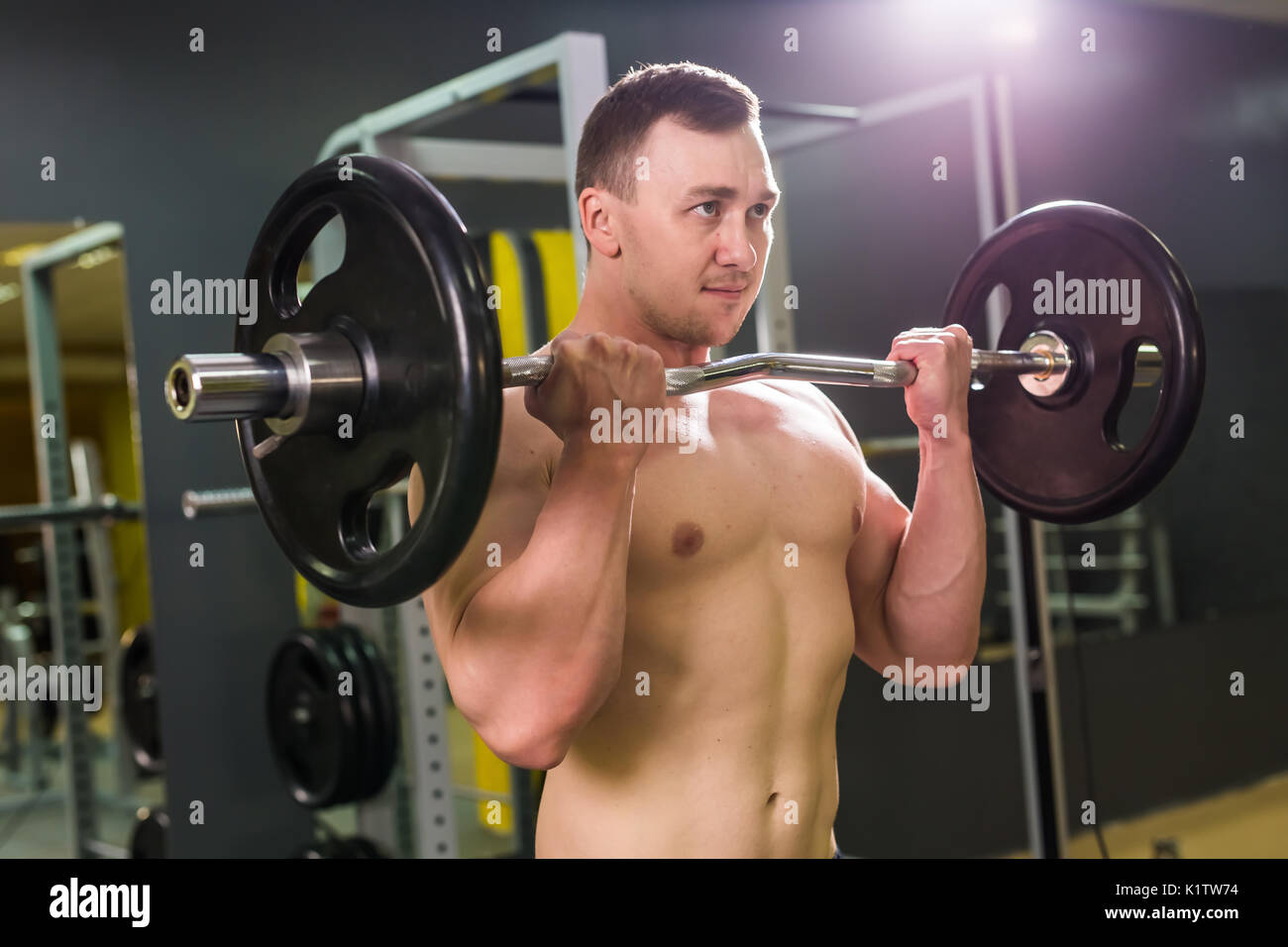 Muscular man with pulling up barbell in fitness training class indoors ...