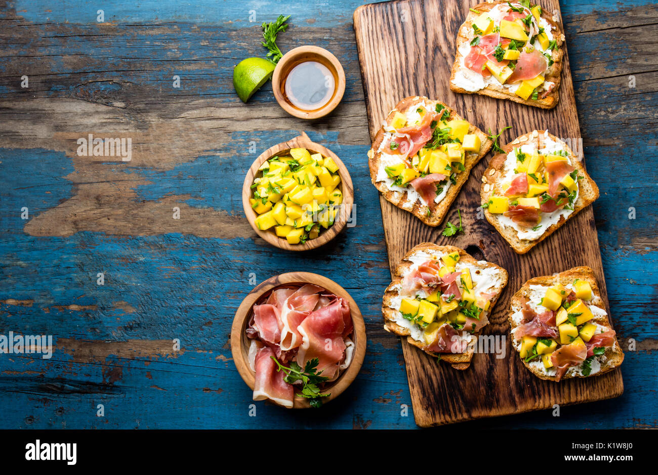 Toasts with cream cheese, ham jamon serrano and mango served on wooden ...