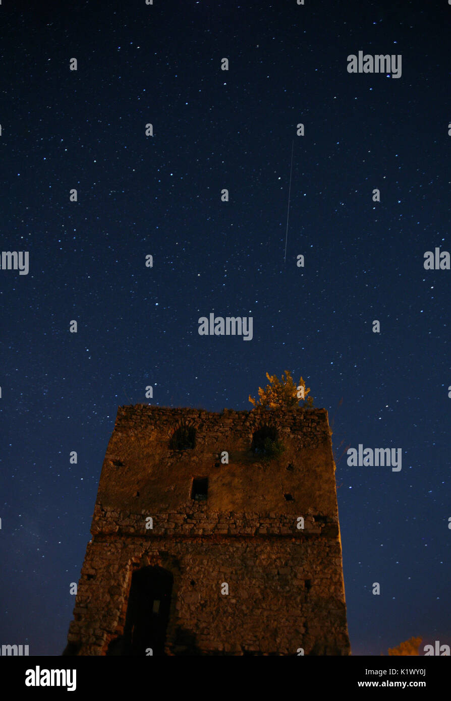 Night starry sky over an abandoned stone tower. A falling star is ...