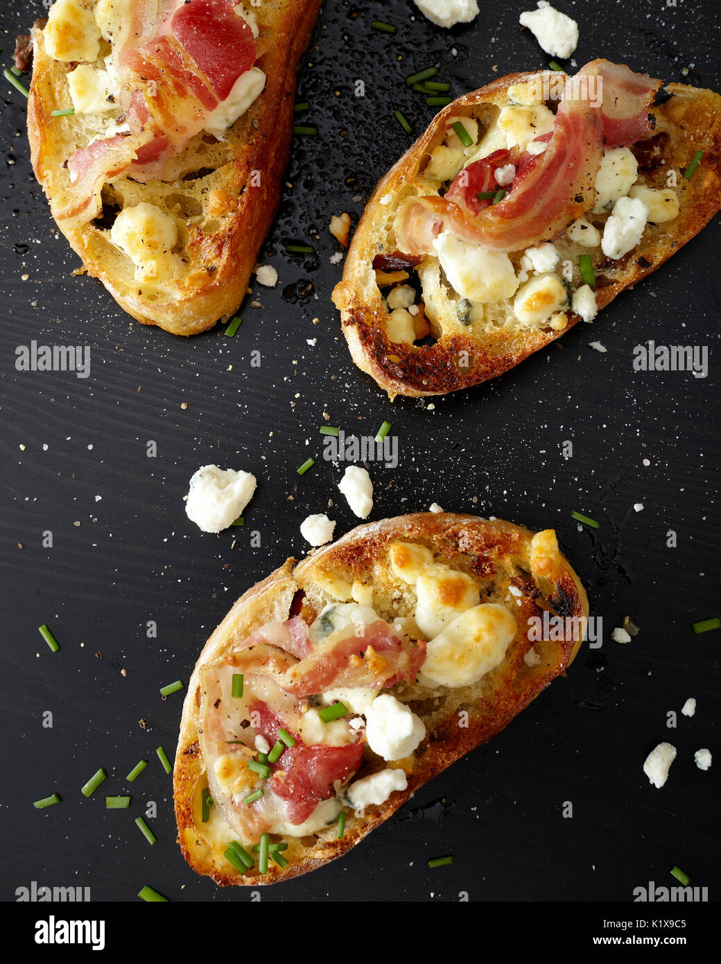 Three toast crustinis with prosciutto, herbs and cheese on a black wood ...