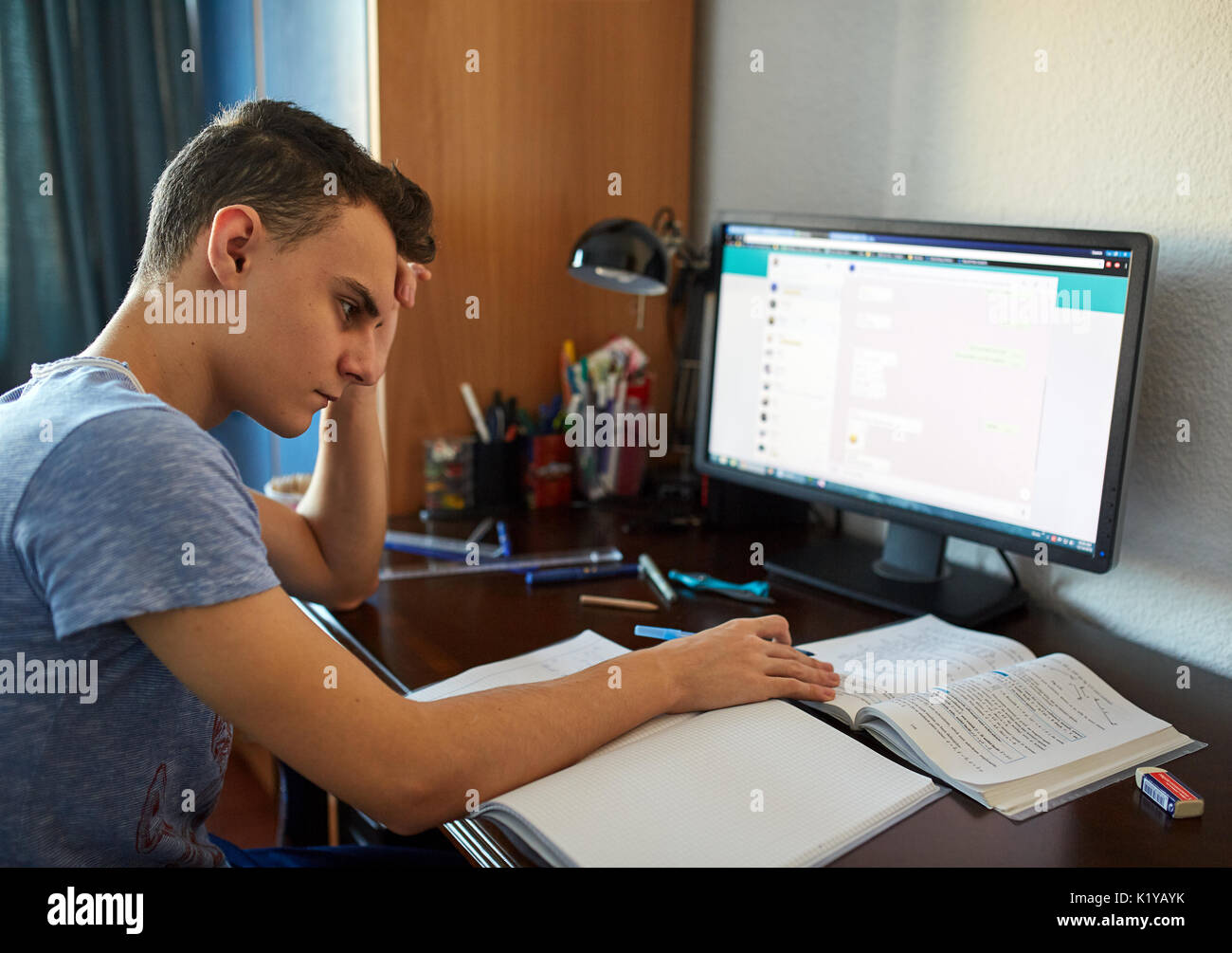 Teenage boy doing homework with computer and books at his desk Stock ...