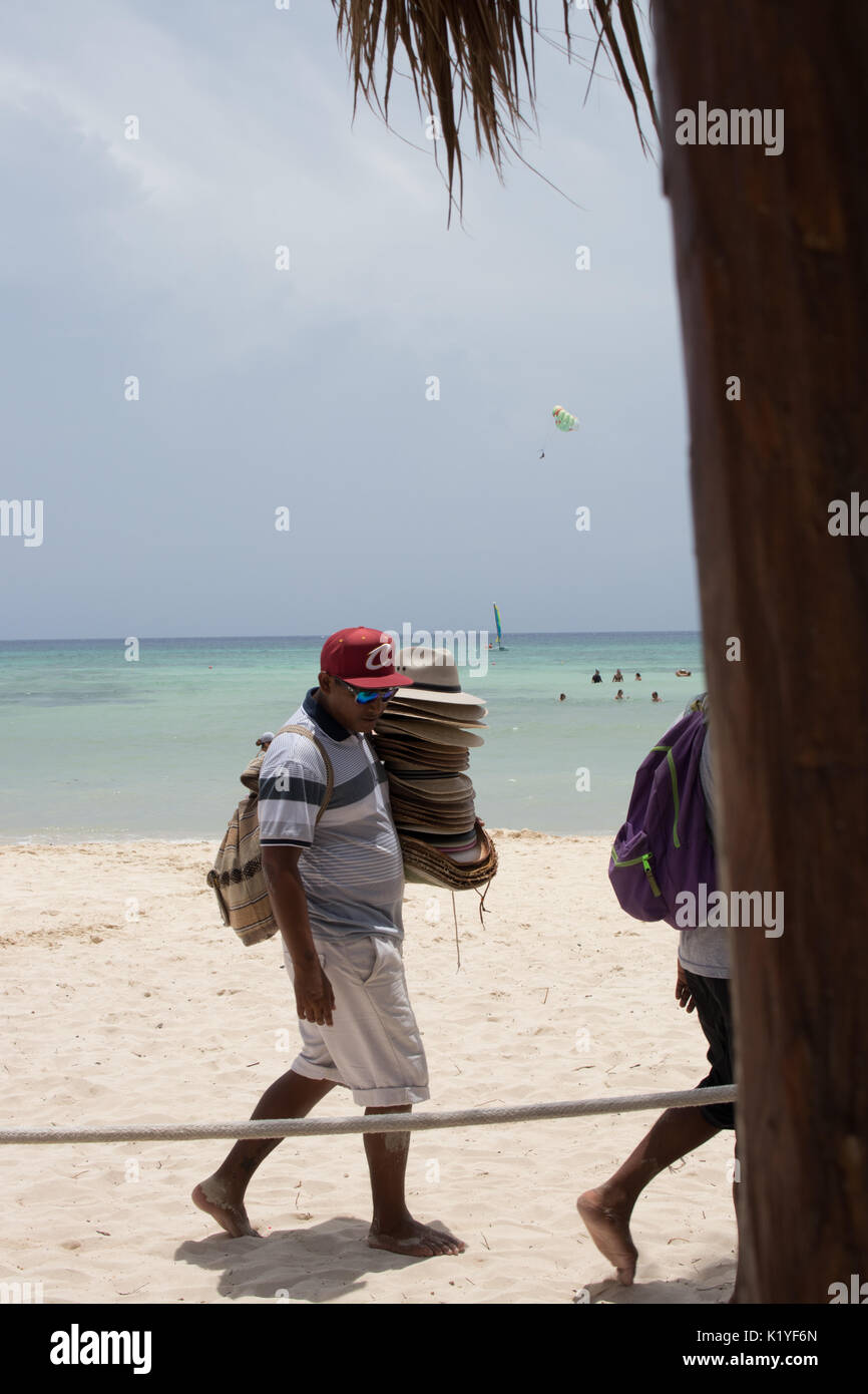 Local traders walking on Caribbean beach carrying piles of hats and ...