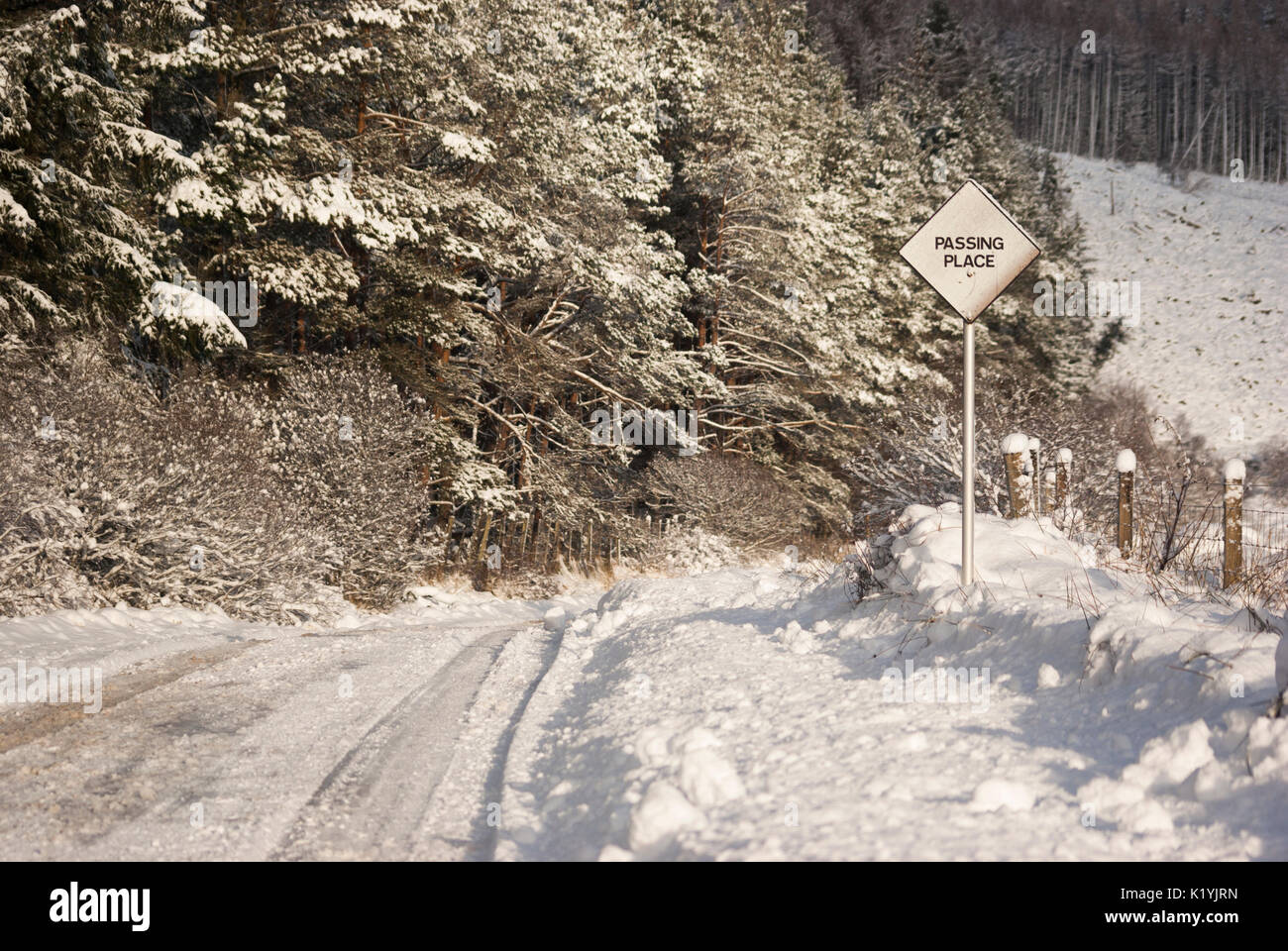 Snow covered road with passing place sign on a clear sunny winters day ...