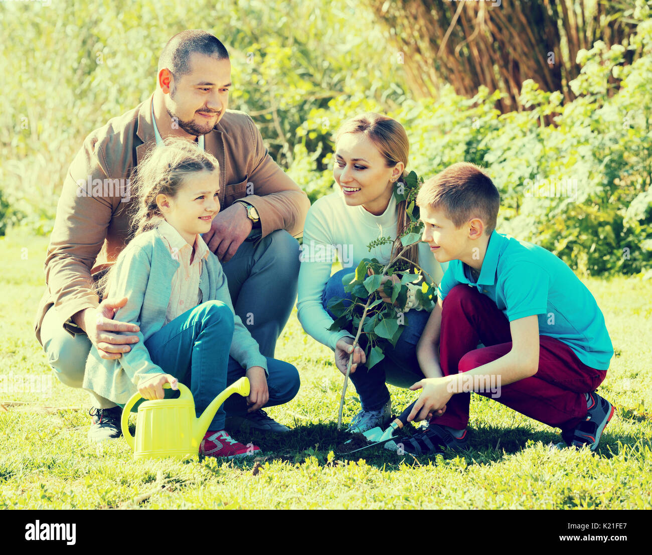 Cheerful young parents with two smiling children planting a tree ...