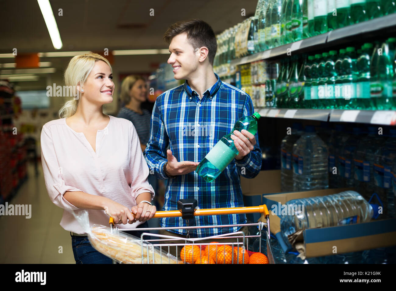 Young smiling customers choosing bottle of sparkling water at ...