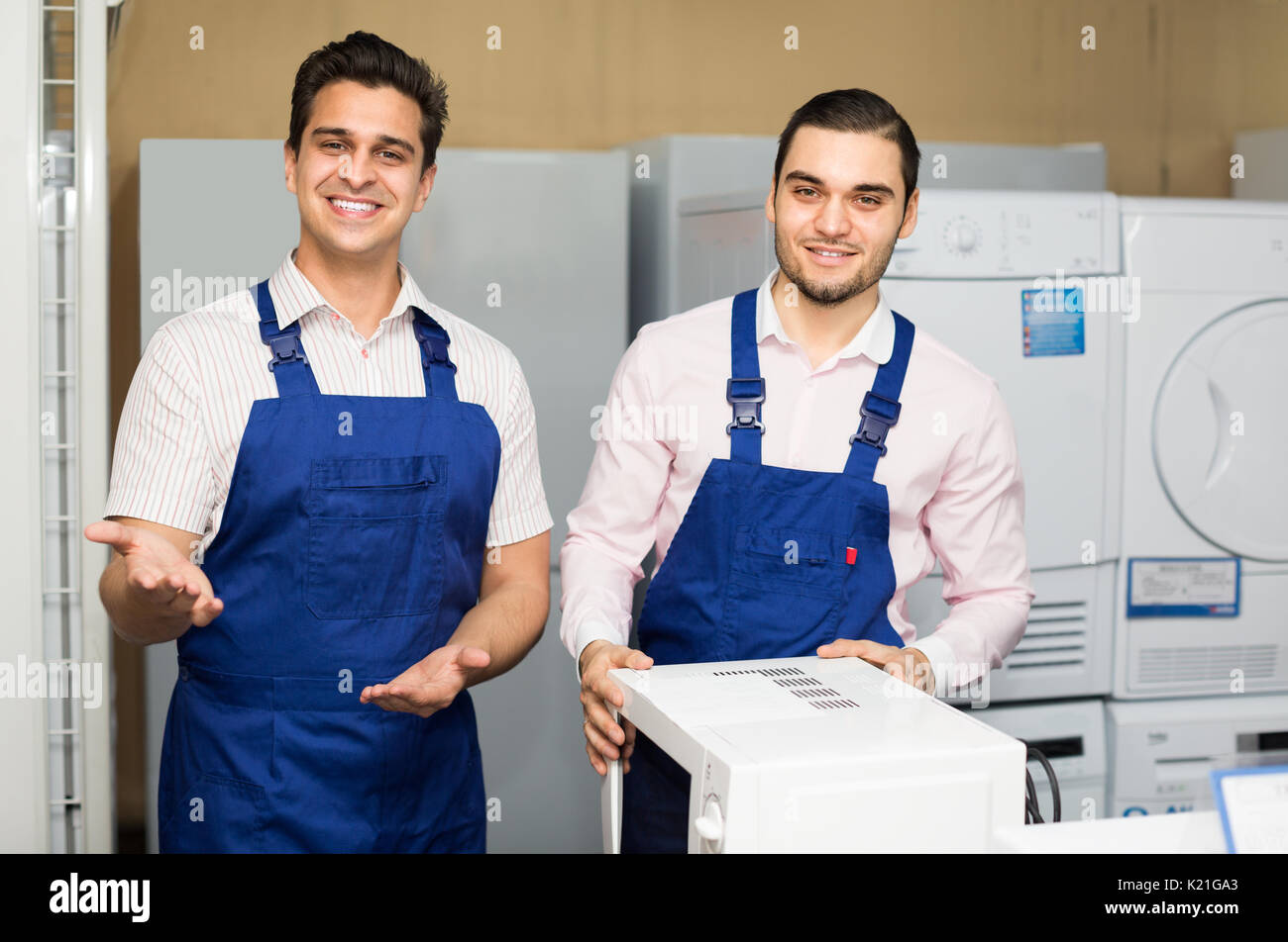 Two workers in blue uniform smiling at household appliances shop Stock ...