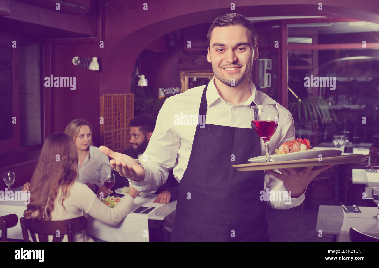 Smiling glad young waiter taking care of adults at cafe table Stock ...