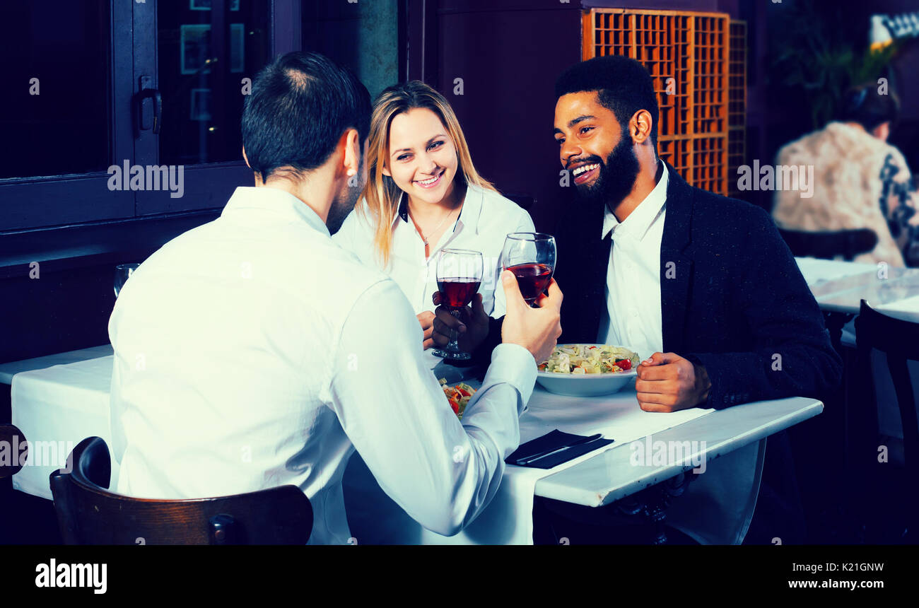 Three positive friends eating at restaurant table and chatting Stock ...