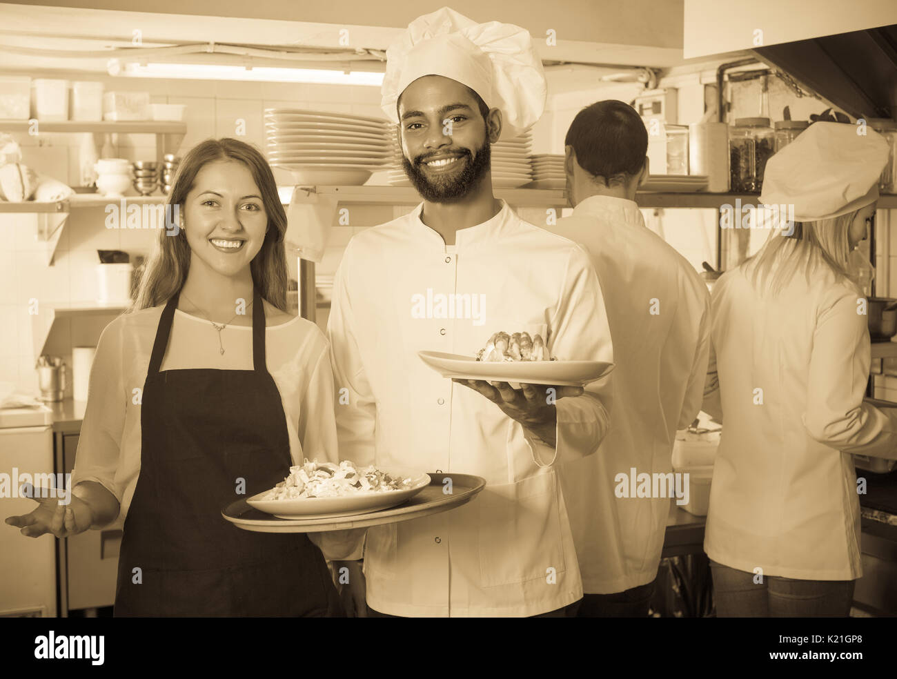 Happy young waitress and cooking team at professional kitchen in ...