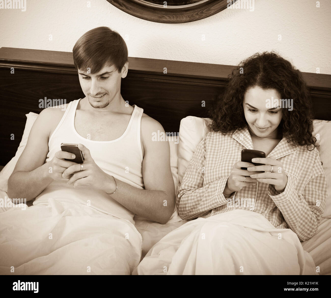 Young addicted couple playing with mobile phones separately in bed ...