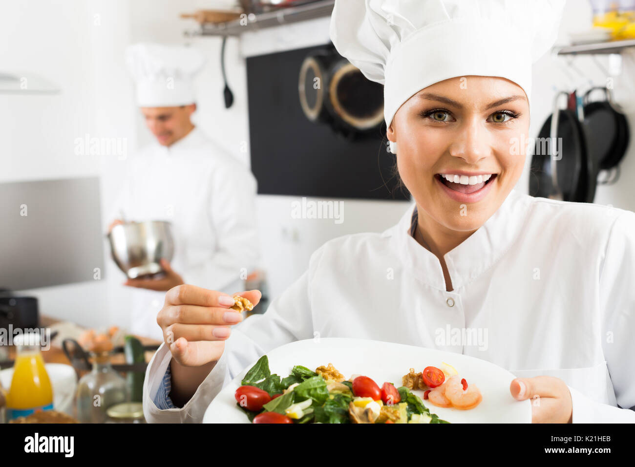 Female cook wearing uniform holding plate with green salad Stock Photo ...