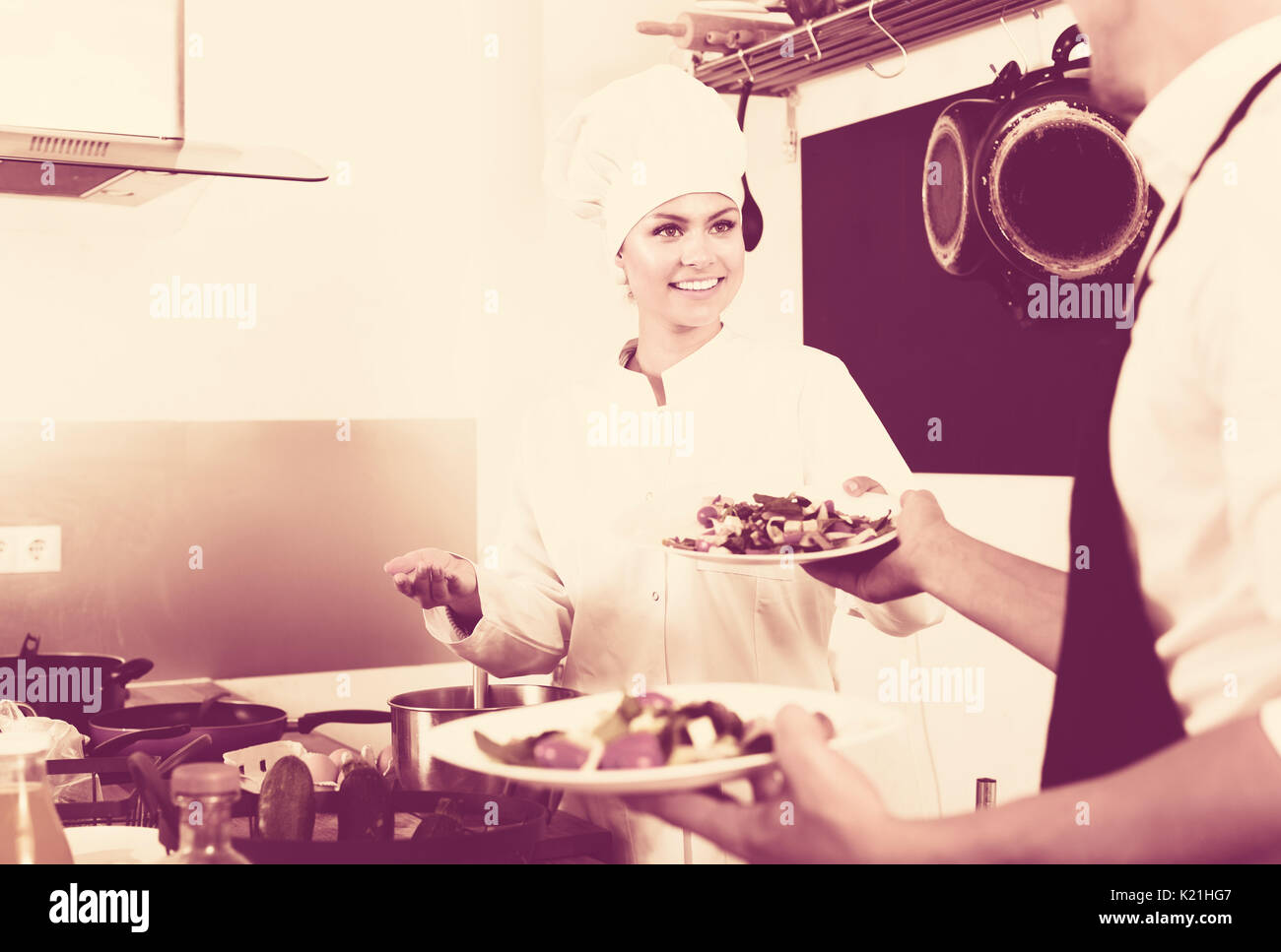 Smiling female cook in uniform standing on kitchen and giving fresh ...