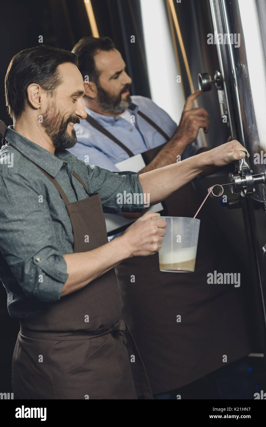 Male brewery worker pouring beer from the tank to plastic pitcher Stock ...