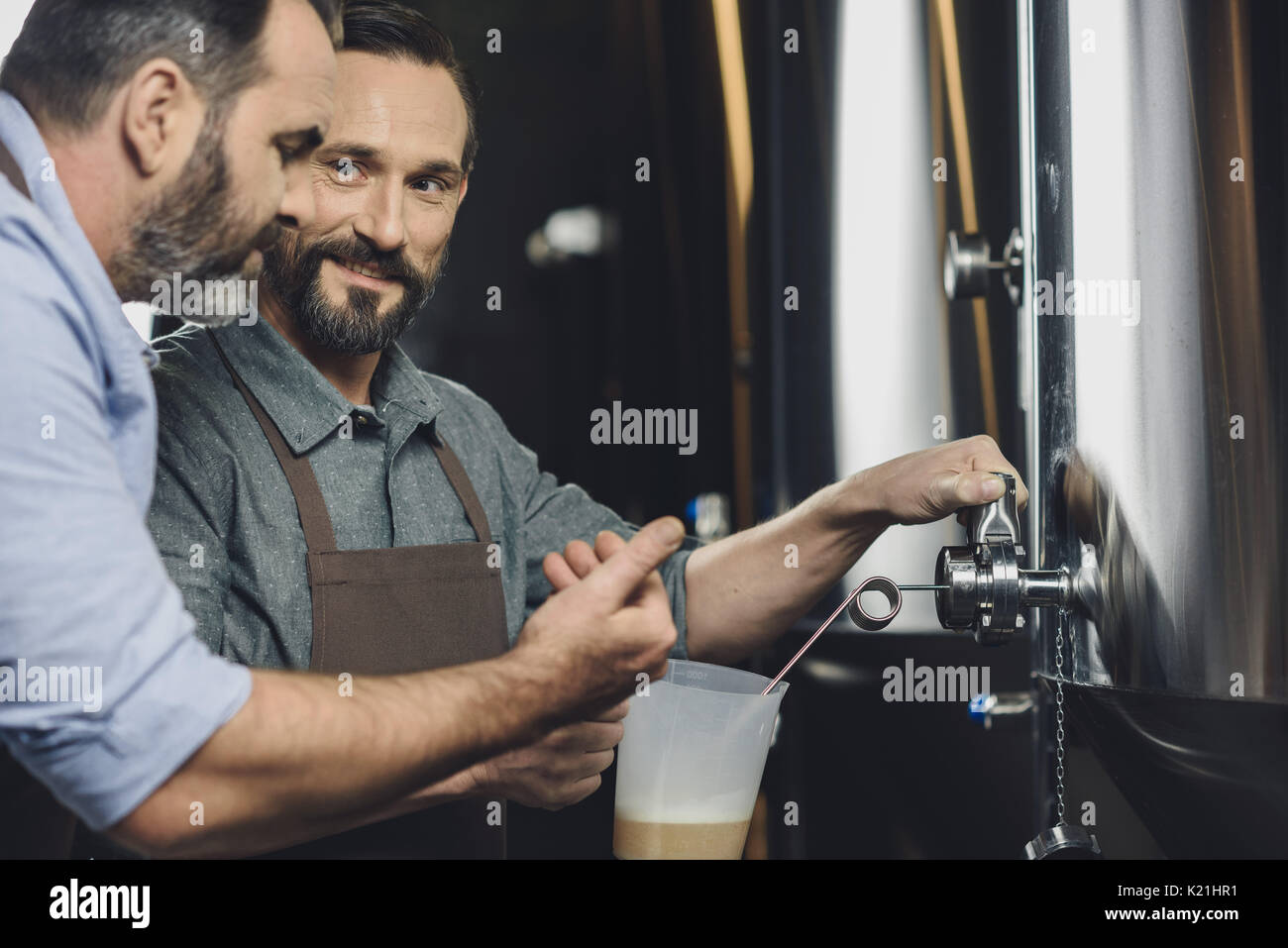 Male brewery workers pouring beer from the tank Stock Photo - Alamy