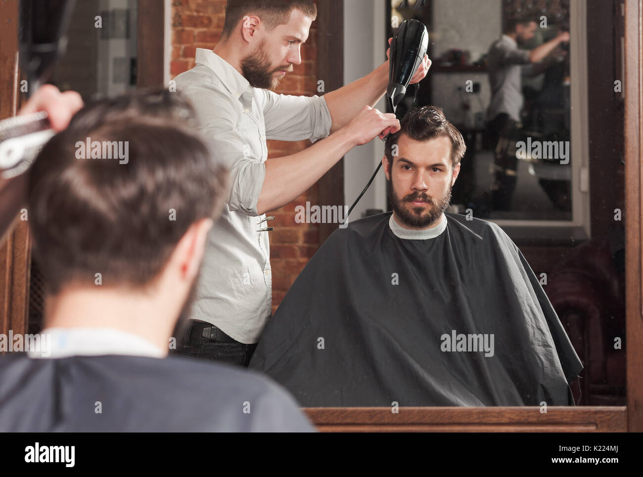Young handsome barber making haircut of attractive man in barbershop ...