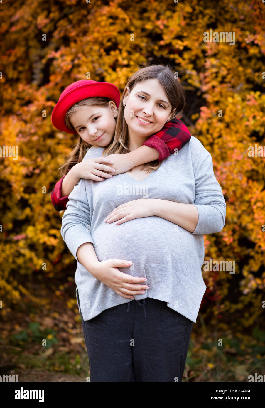 Happy young pregnant mother hugging with teen daughter in autumn park ...
