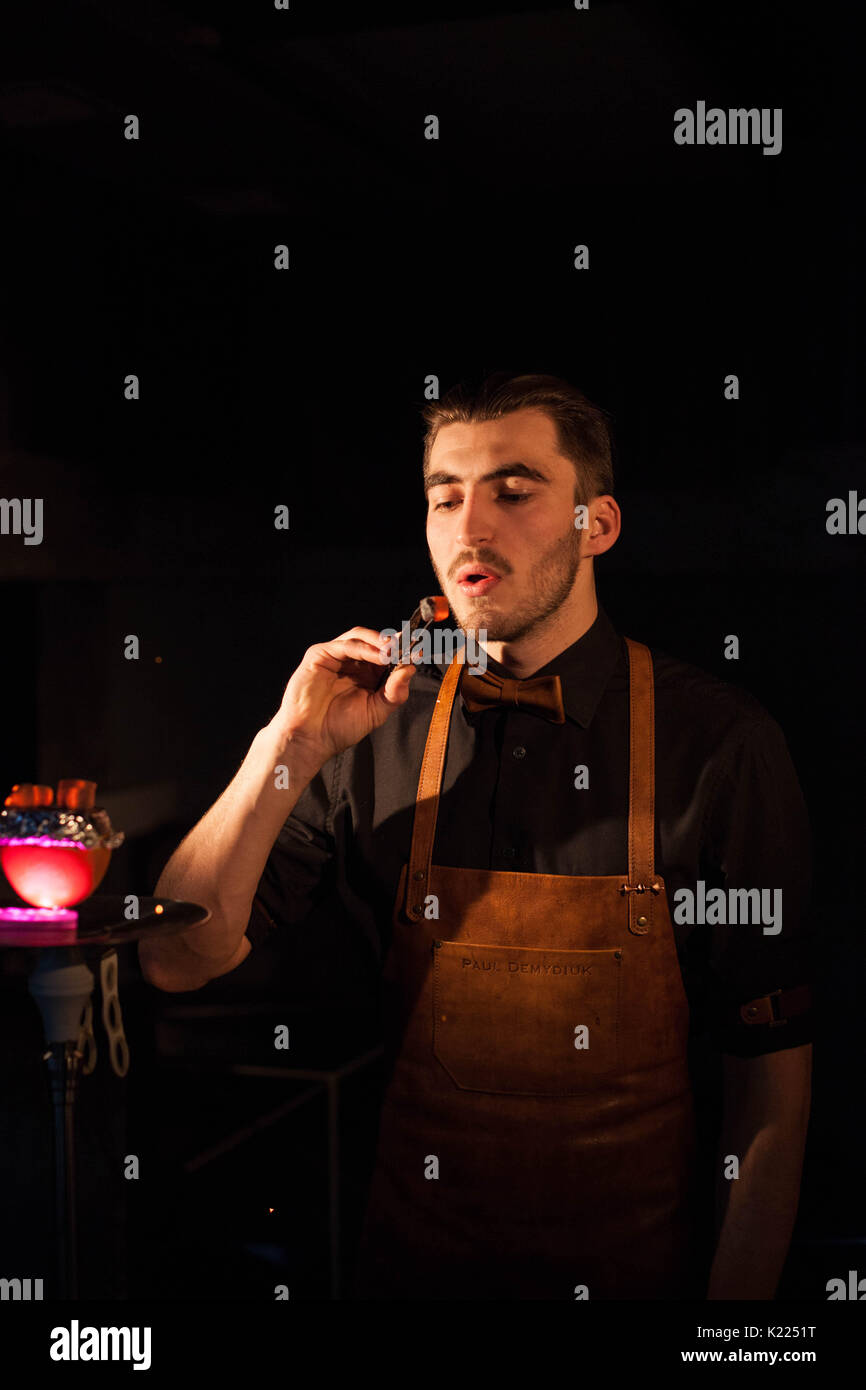 Shisha man standing near the big hookah and blowing on a hookah ember ...