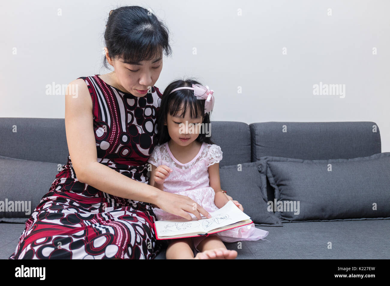 Asian Chinese mother and daughter reading the book on sofa at home ...