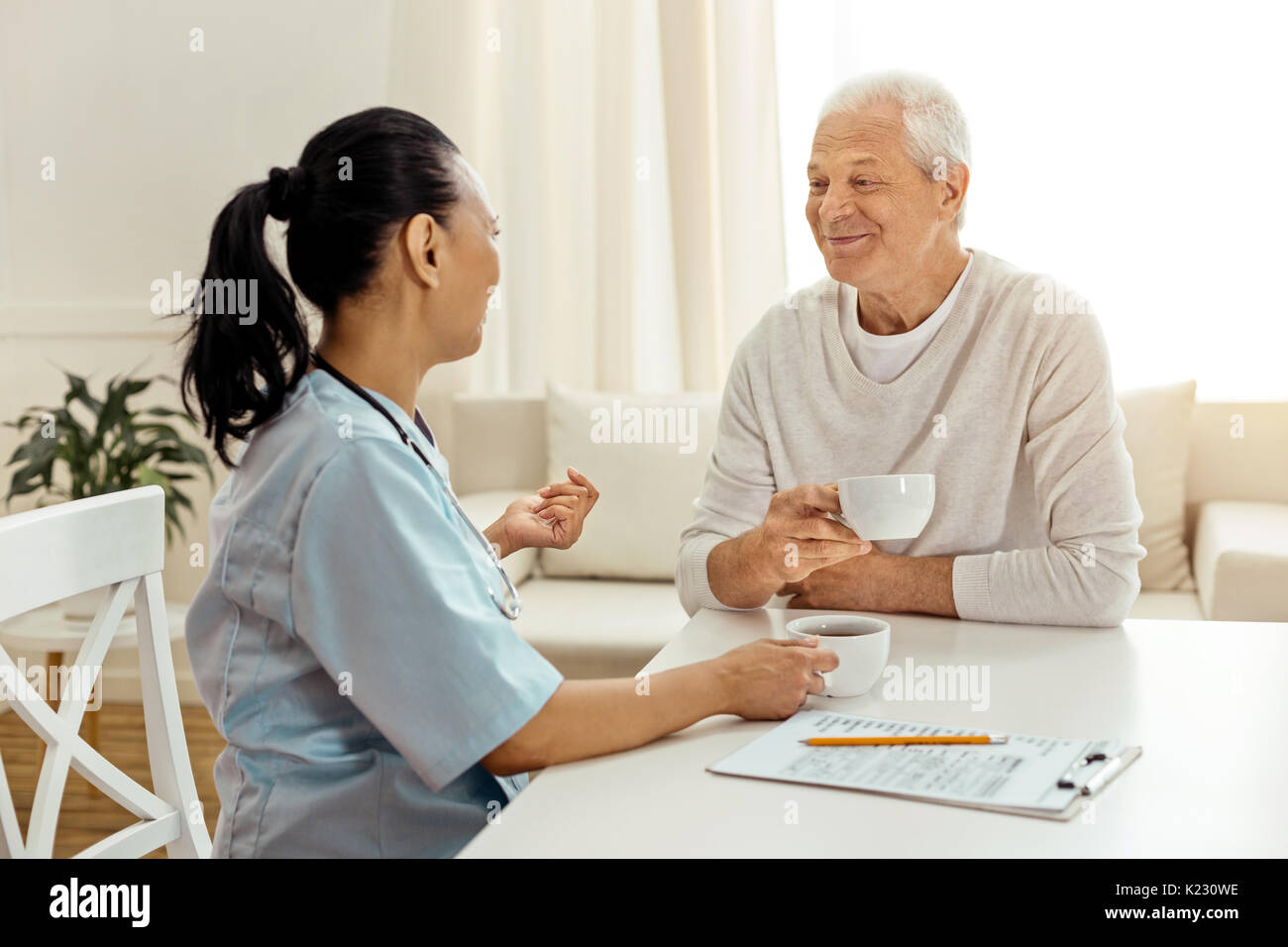 Positive nice caregiver and patient having tea Stock Photo - Alamy