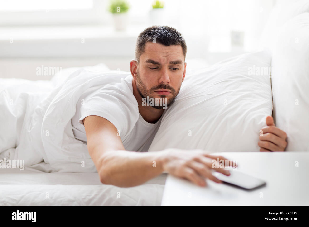 young man reaching for smartphone in bed Stock Photo - Alamy