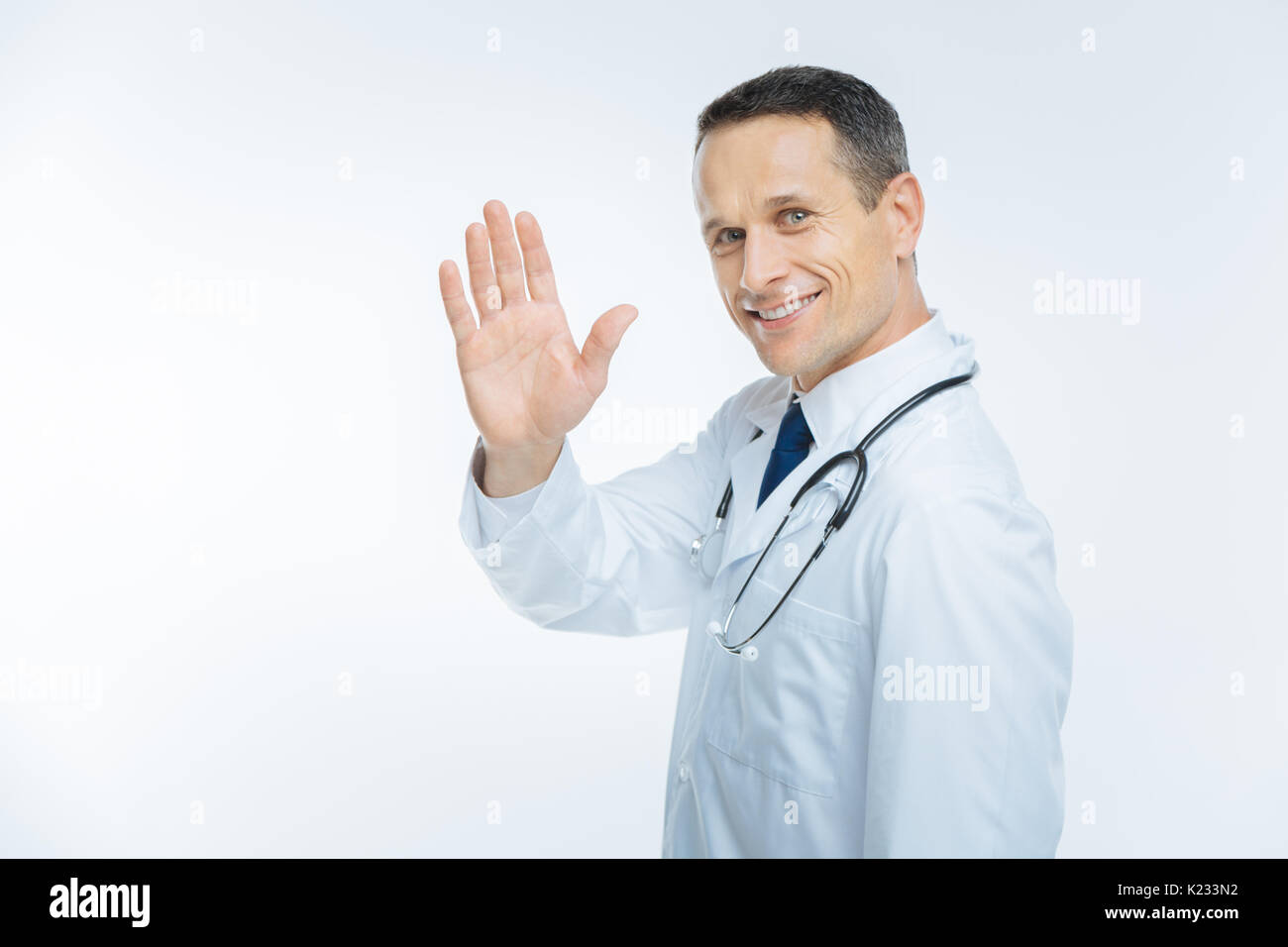 Positive minded mature doctor waving hello over background Stock Photo ...