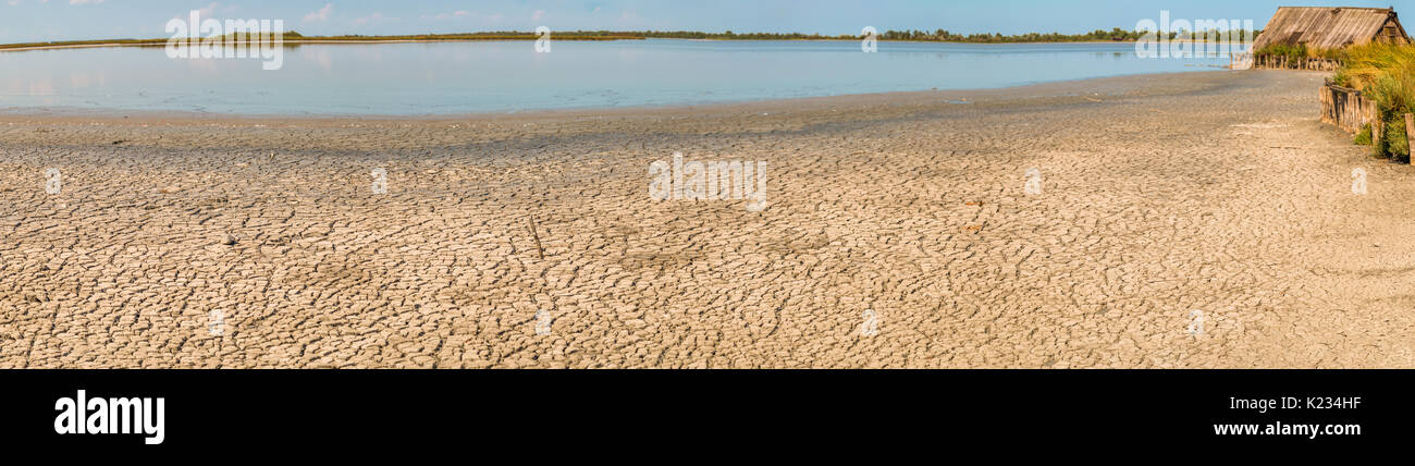 cracked clay soil beach with a straw hut on clear lagoon water Stock ...