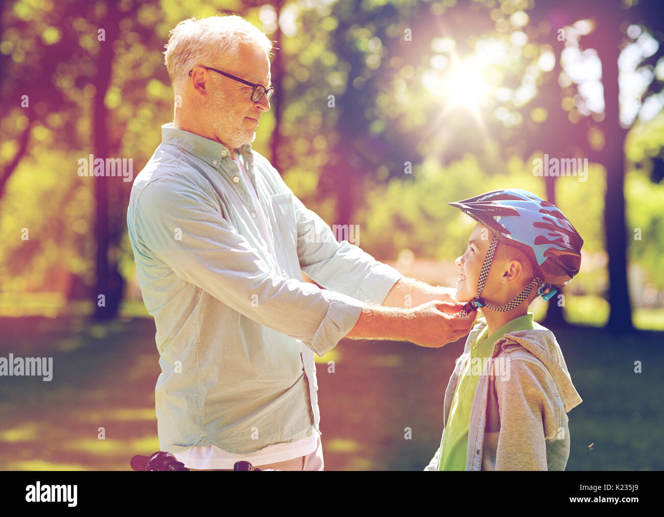 old man helping boy with bike helmet at park Stock Photo - Alamy