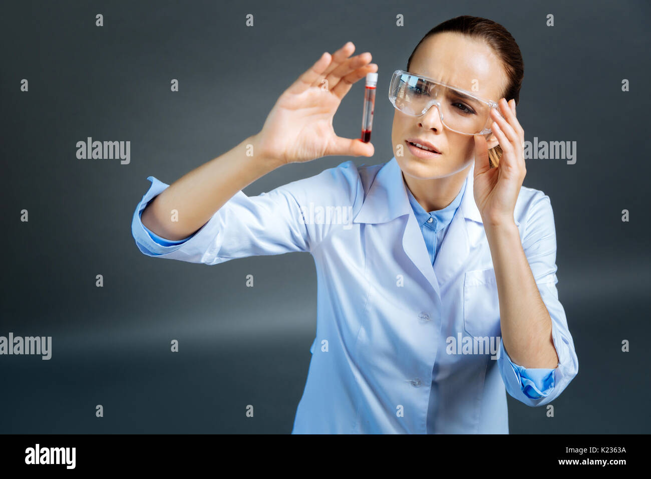 Confused female doctor looking at glass tube with blood Stock Photo - Alamy