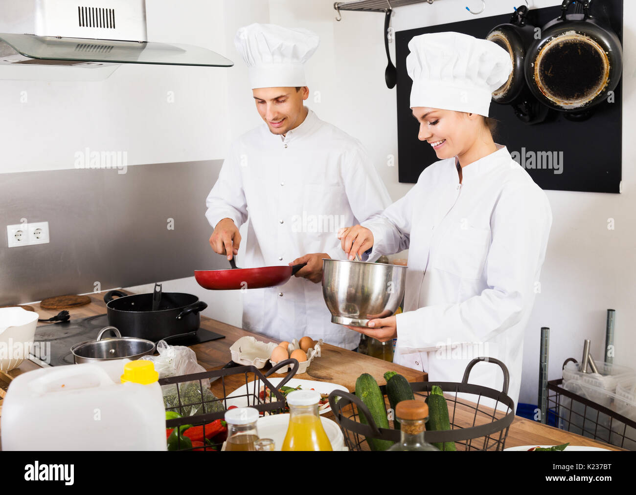 Two glad young man and woman chefs cooking food at restaurant's kitchen ...