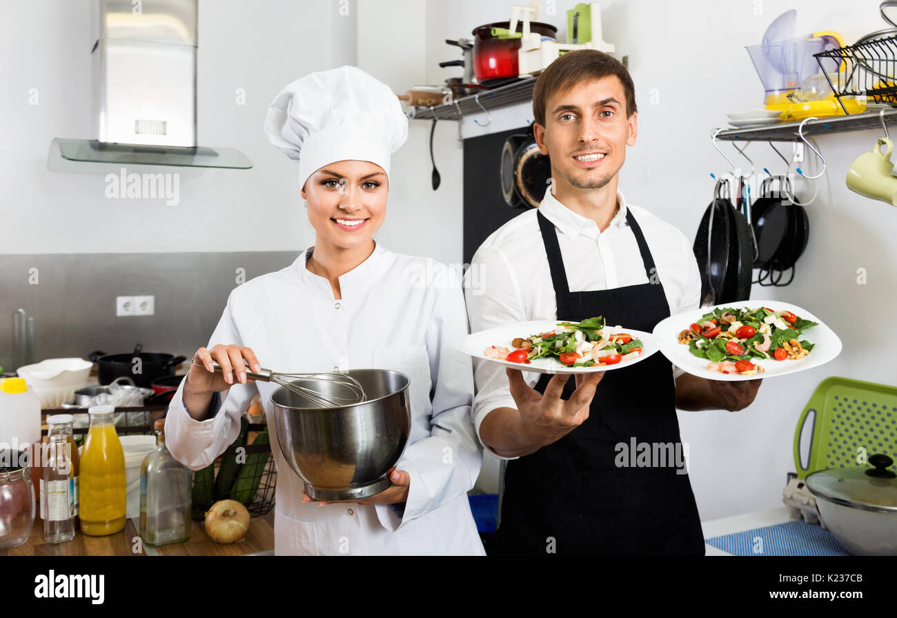 Portrait of young smiling pleasant cook giving to waitress ready to ...