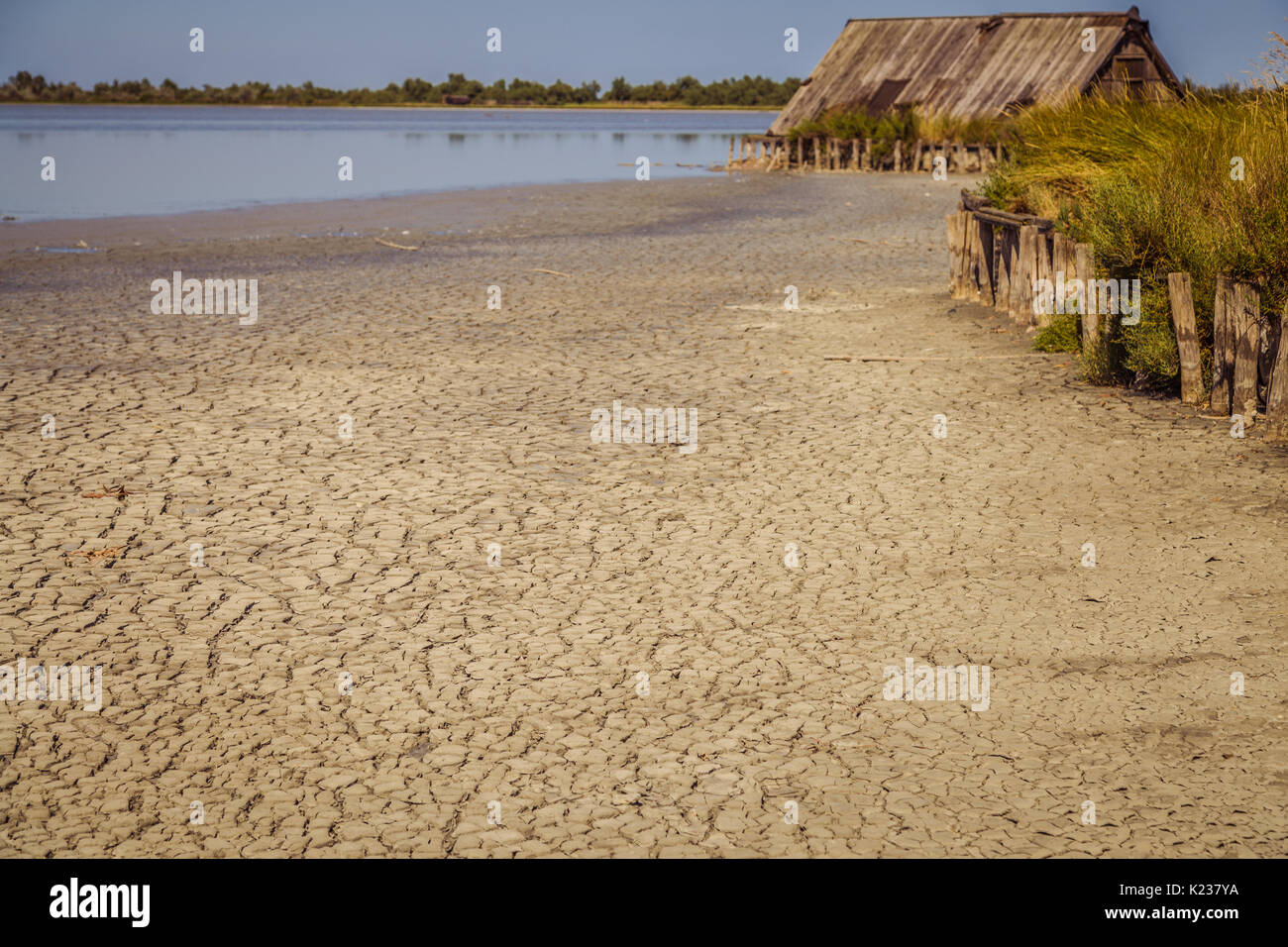 cracked clay soil beach with a straw hut on clear lagoon water Stock ...